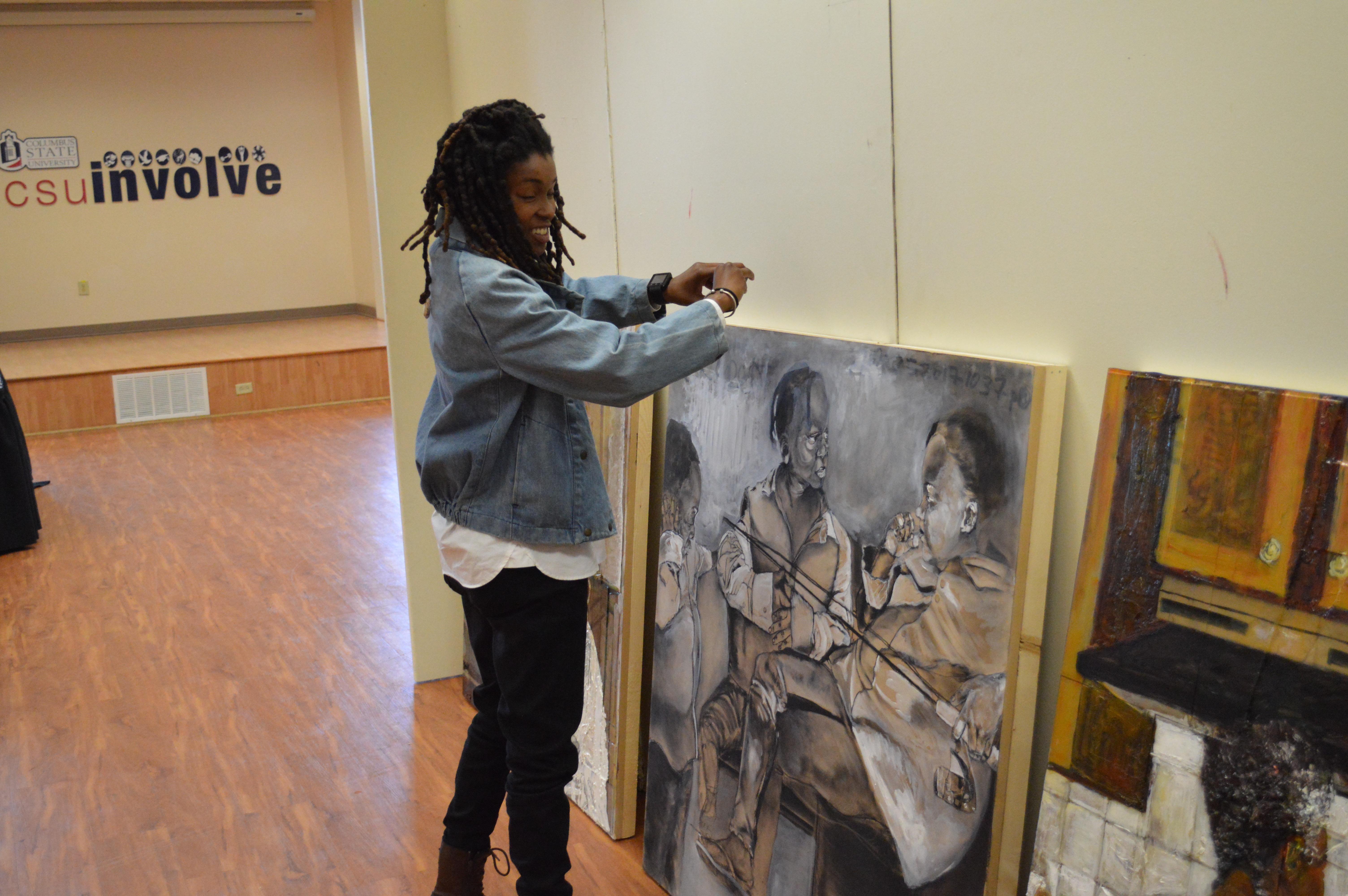 A smiling student preparing to hang her paintings